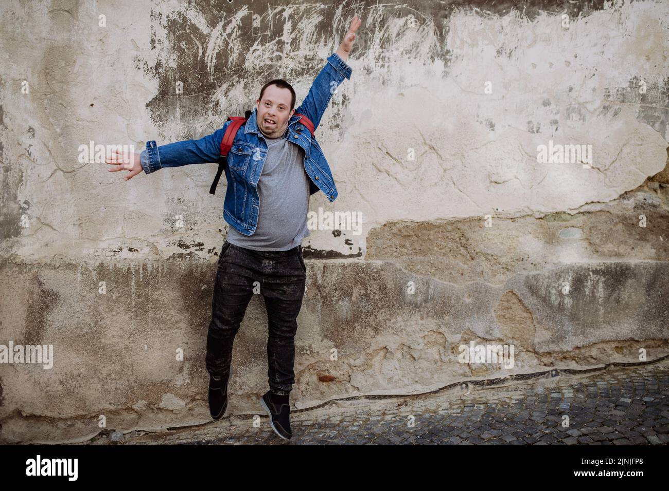 Cheerful young man with Down sydrome jumping in the street, in front of ...