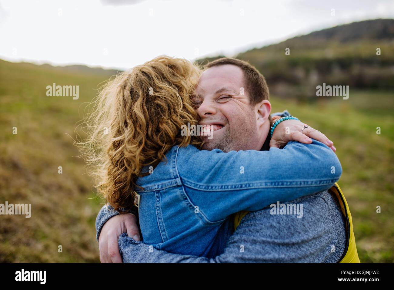 Outdoor portrait of mother hugging her grown up son with Down syndrome ...