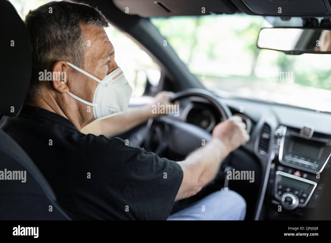 Senior in his 70s driving a car wearing face mask for protection ...