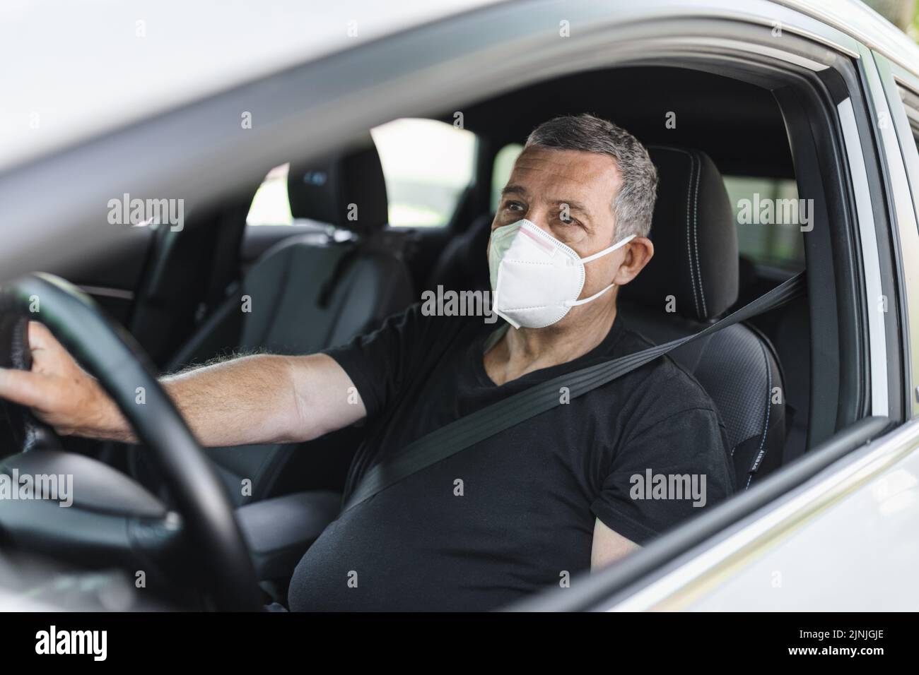 Senior in his 70s driving a car wearing face mask for protection ...