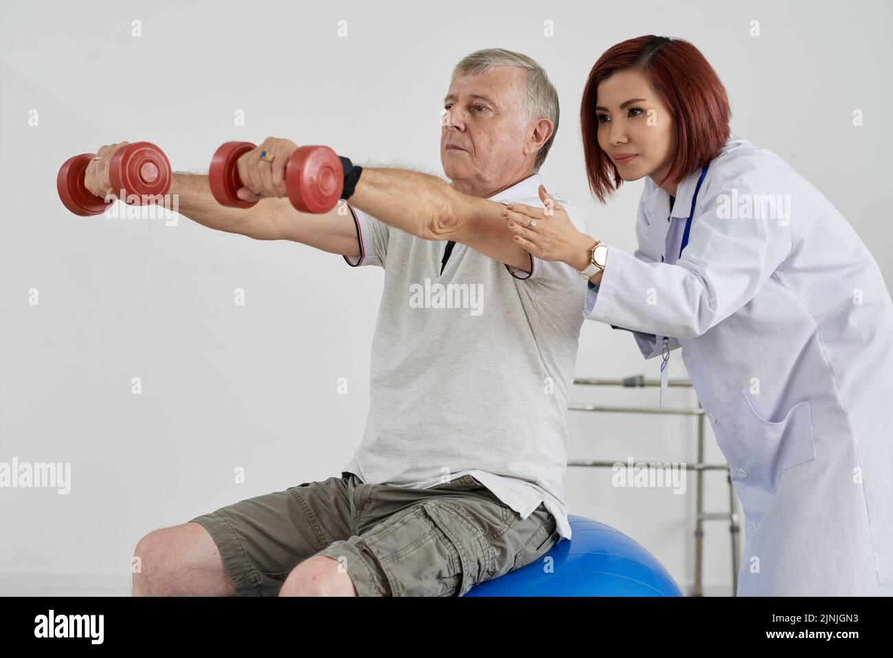 Physioterapist controlling how aged man exercising with dumbbells Stock ...