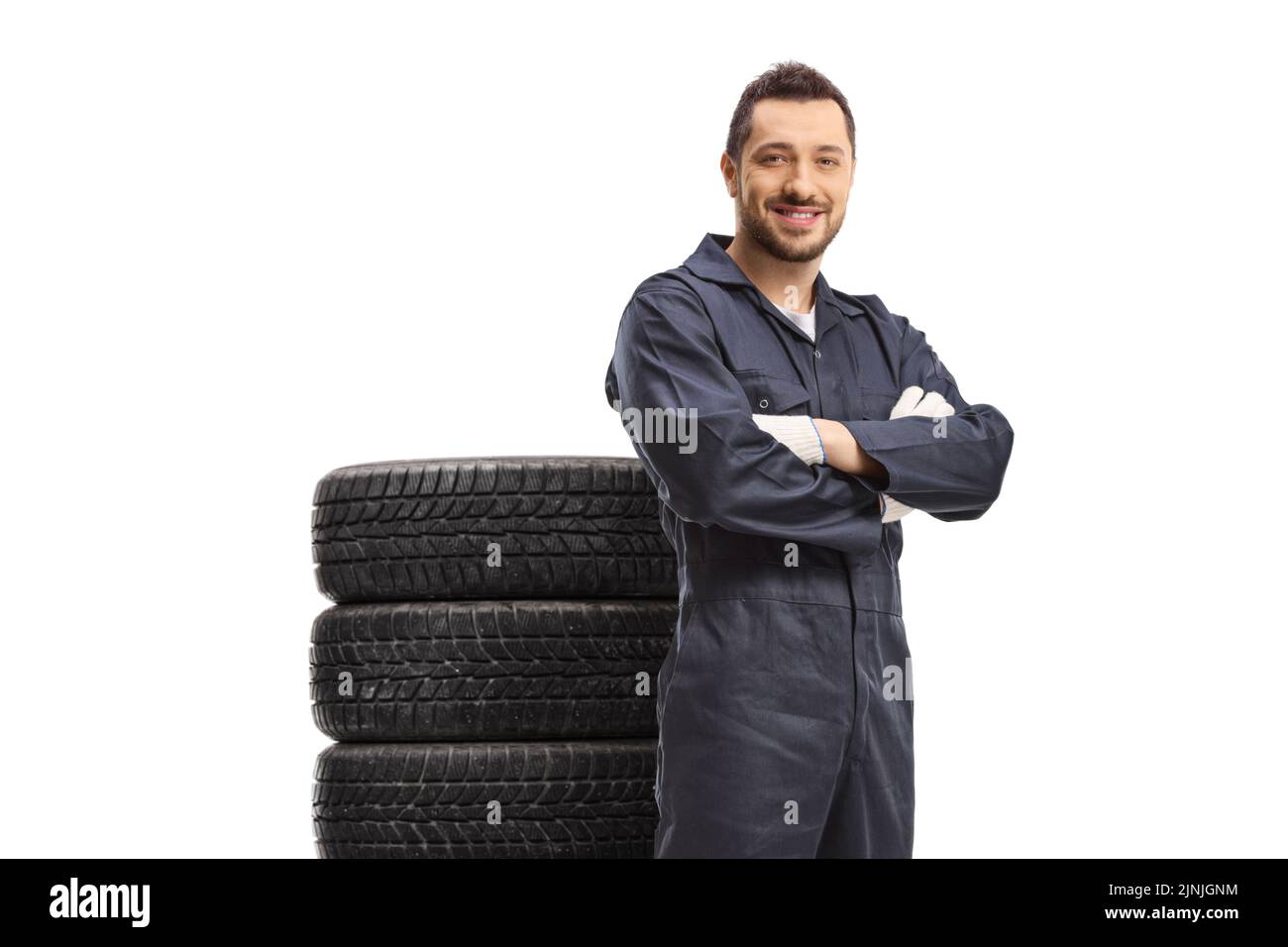Smiling car mechanic posing with a pile of tires behind him isolated on ...