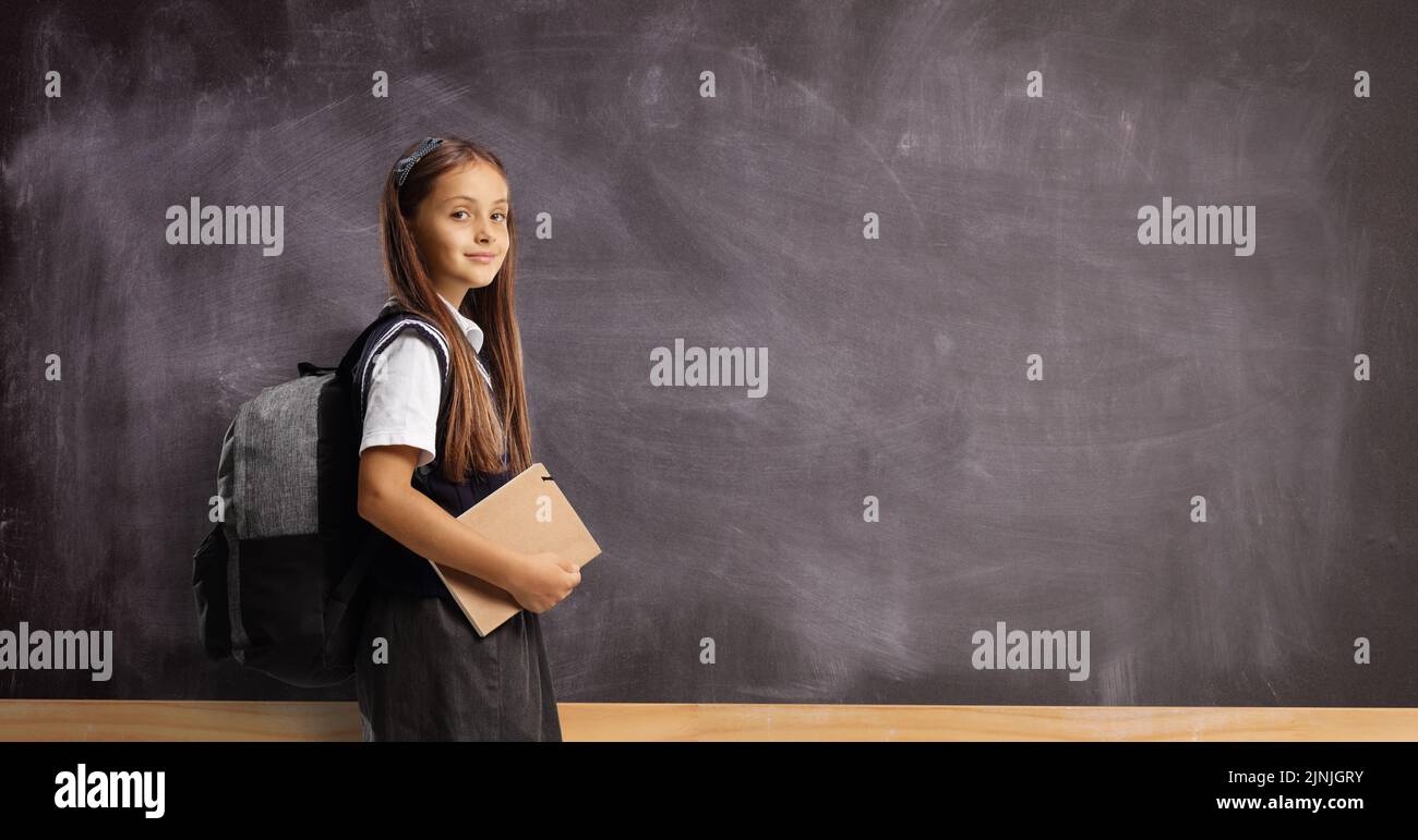 Schoolgirl with a backpack and book standing in front of a blank ...