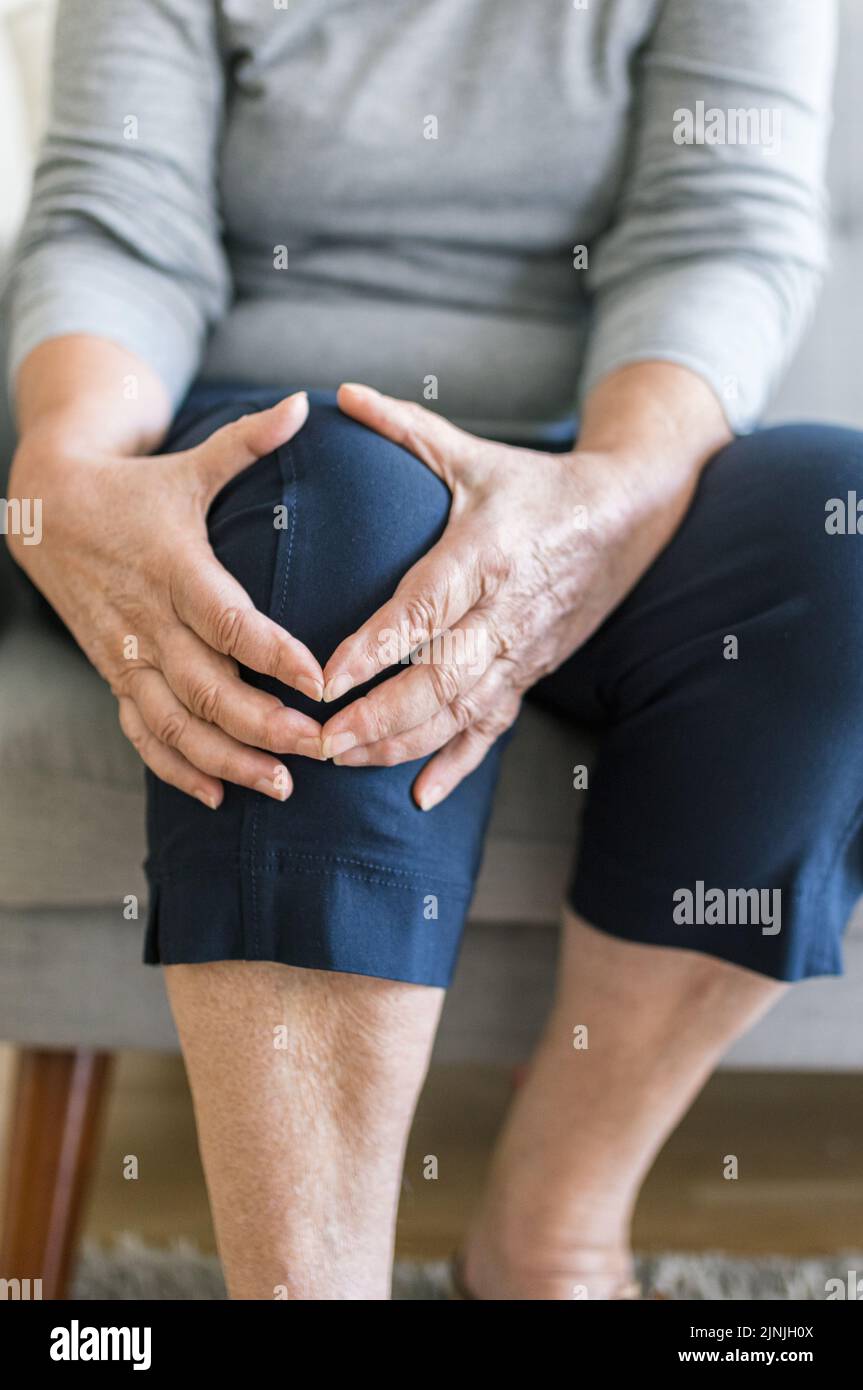 Senior woman sitting on bench, holding her painful knee Stock Photo - Alamy