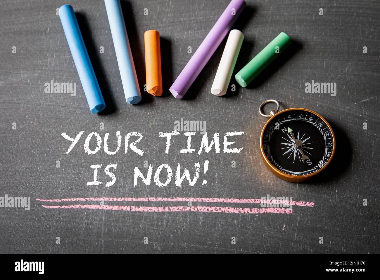 Your time is now. Compass and colorful pieces of chalk on blackboard ...