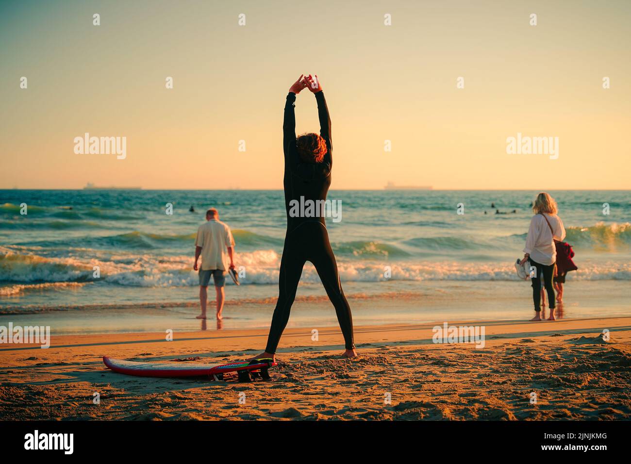 A slim surfer stretching at the beach with foamy waves at sunset Stock ...