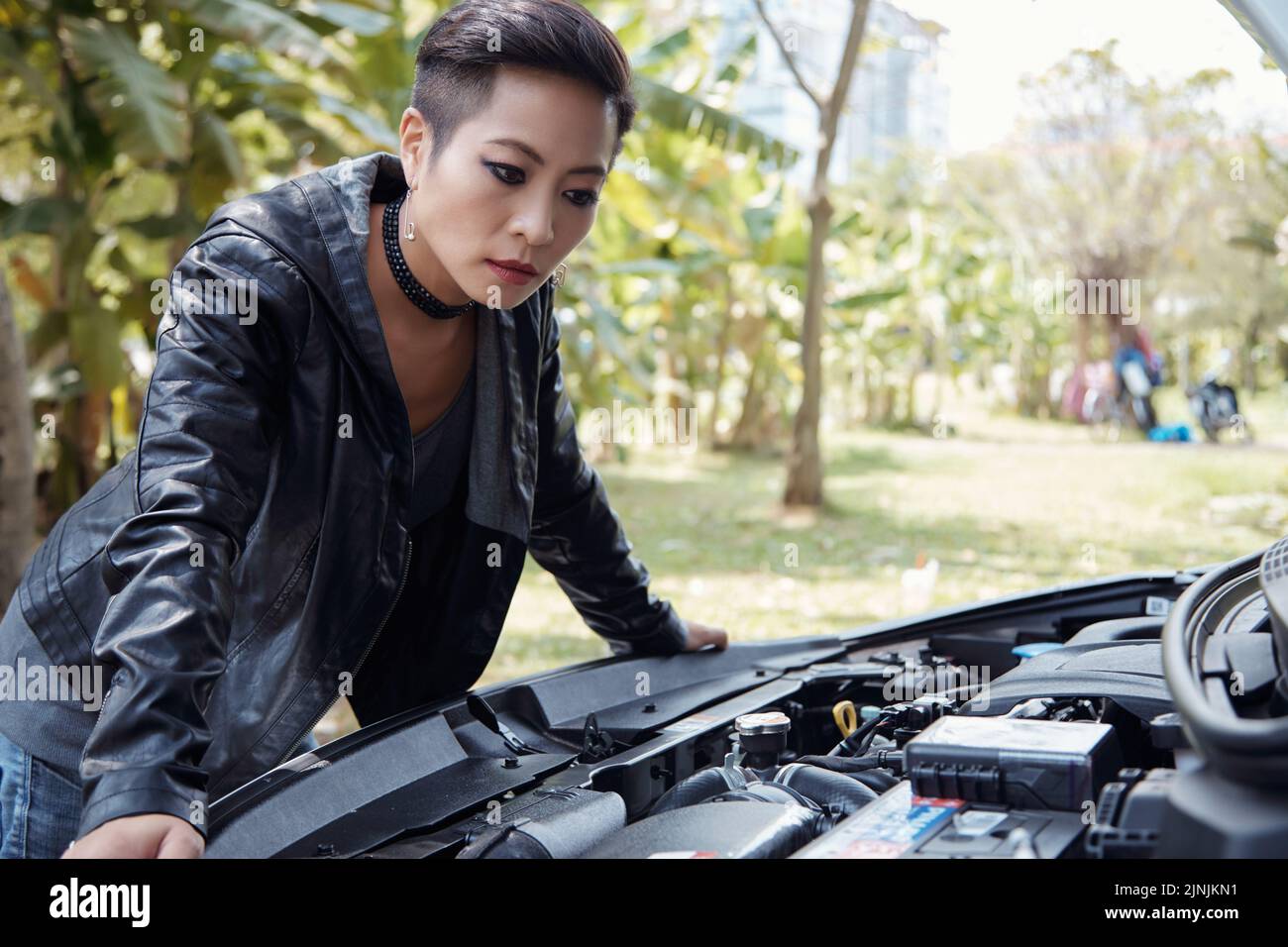 Serious woman looking under the hood of her car Stock Photo - Alamy