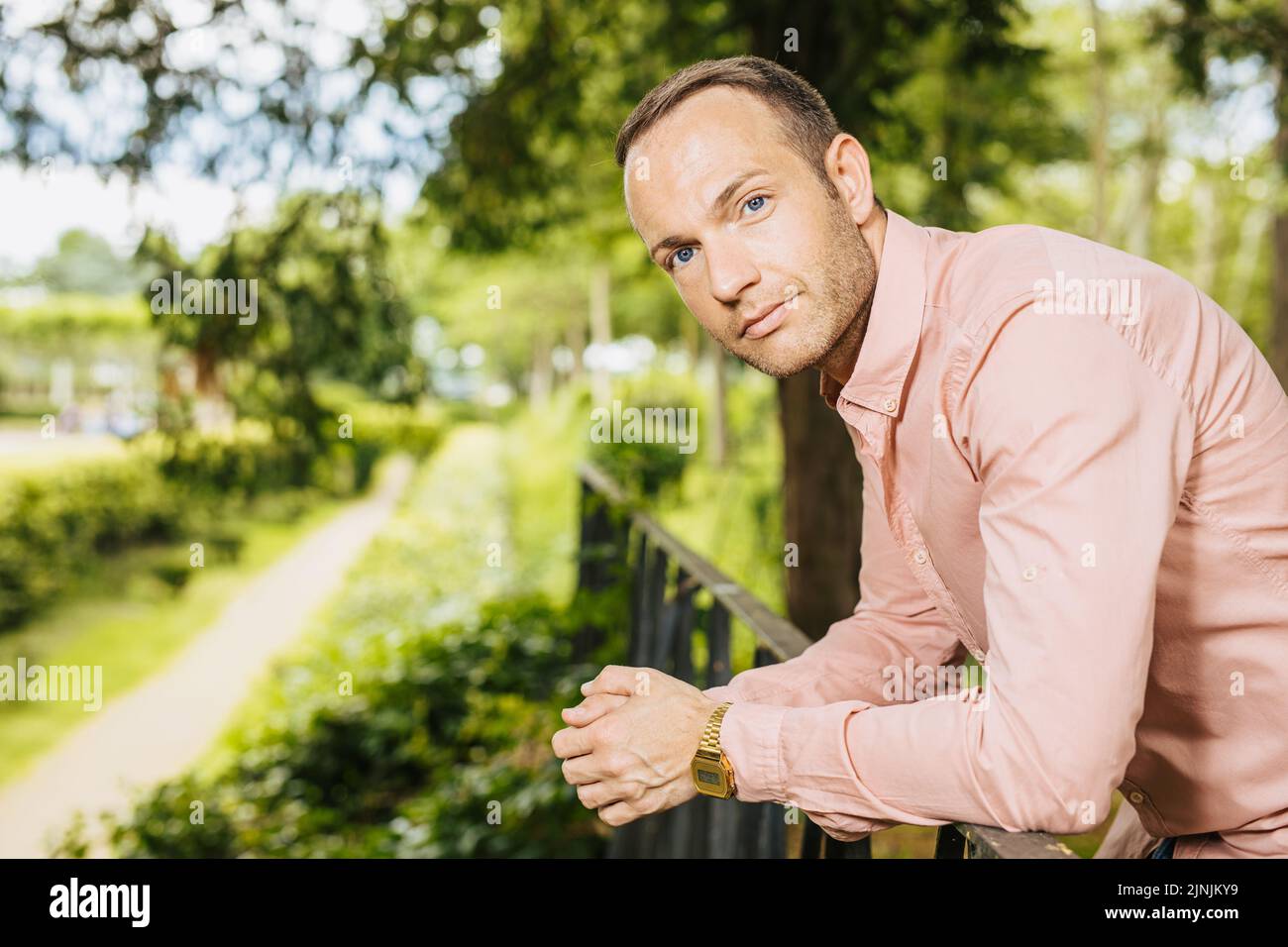 A shallow focus shot of an adult male leaning on a metallic fence with ...