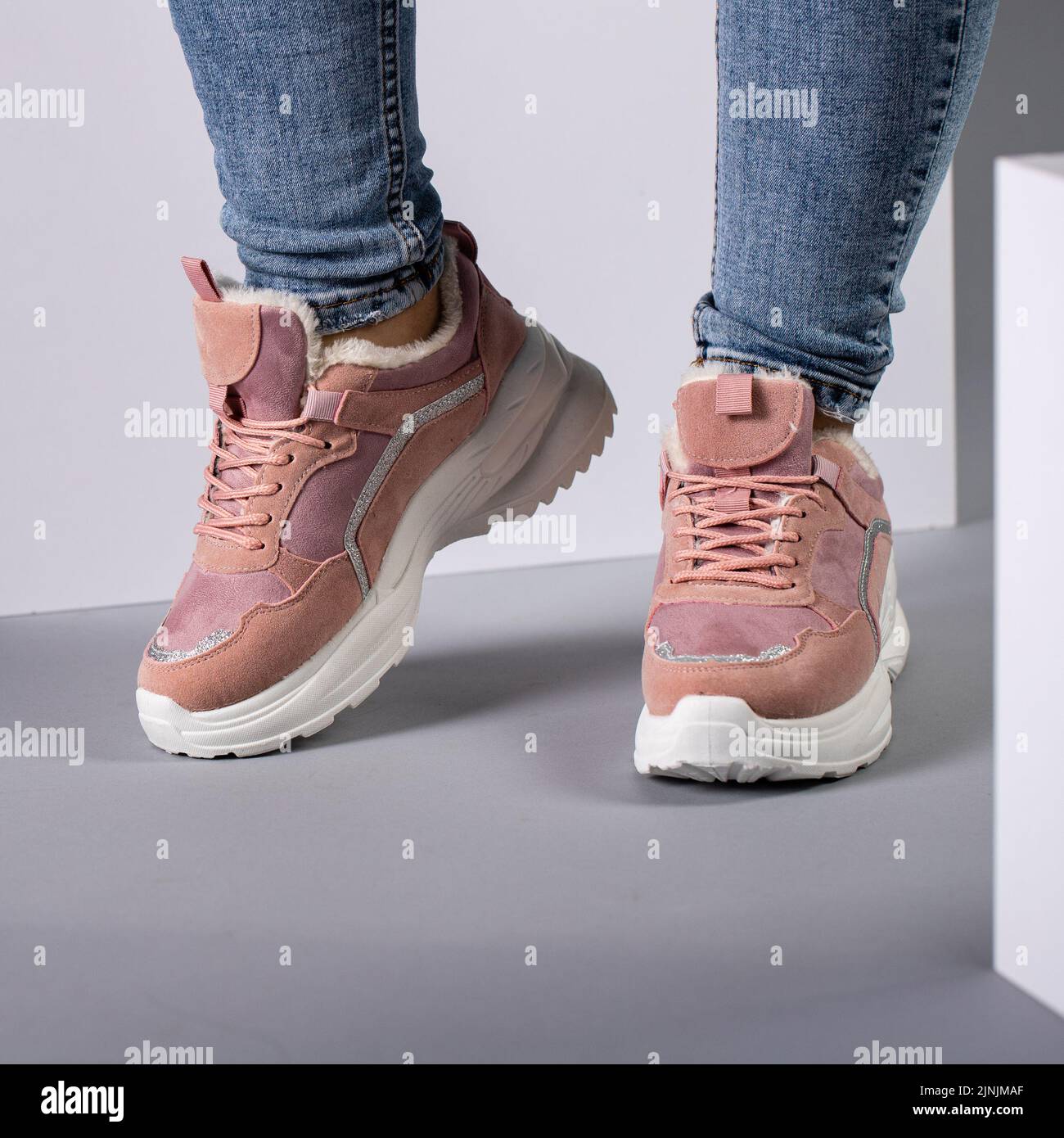 Cropped image of warm pink sneakers with down on female model legs in ...