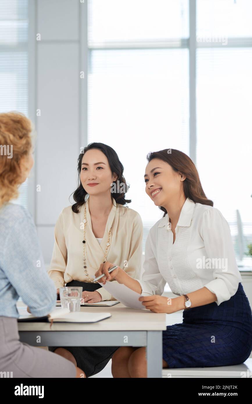 Cheerful beautiful Asian business women explaining idea to partner ...