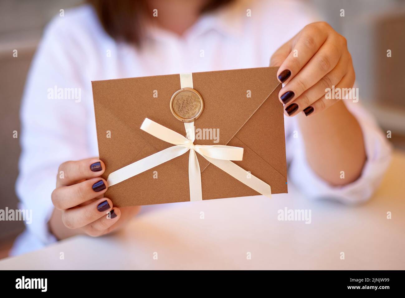 close-up photo of female hands holding bronze invitation envelope with ...