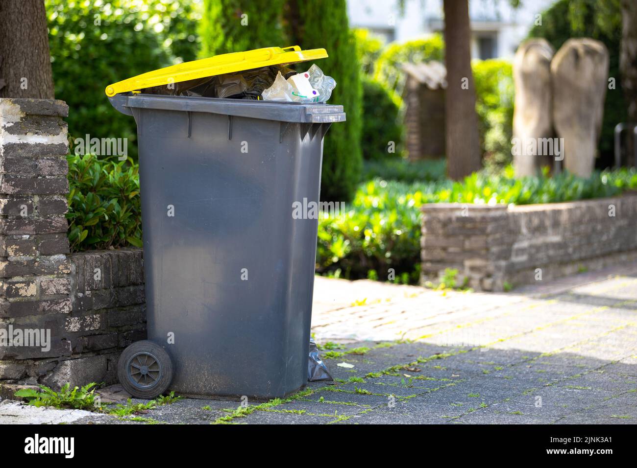 A full garbage trash standing at sidewalk next to street Stock Photo ...