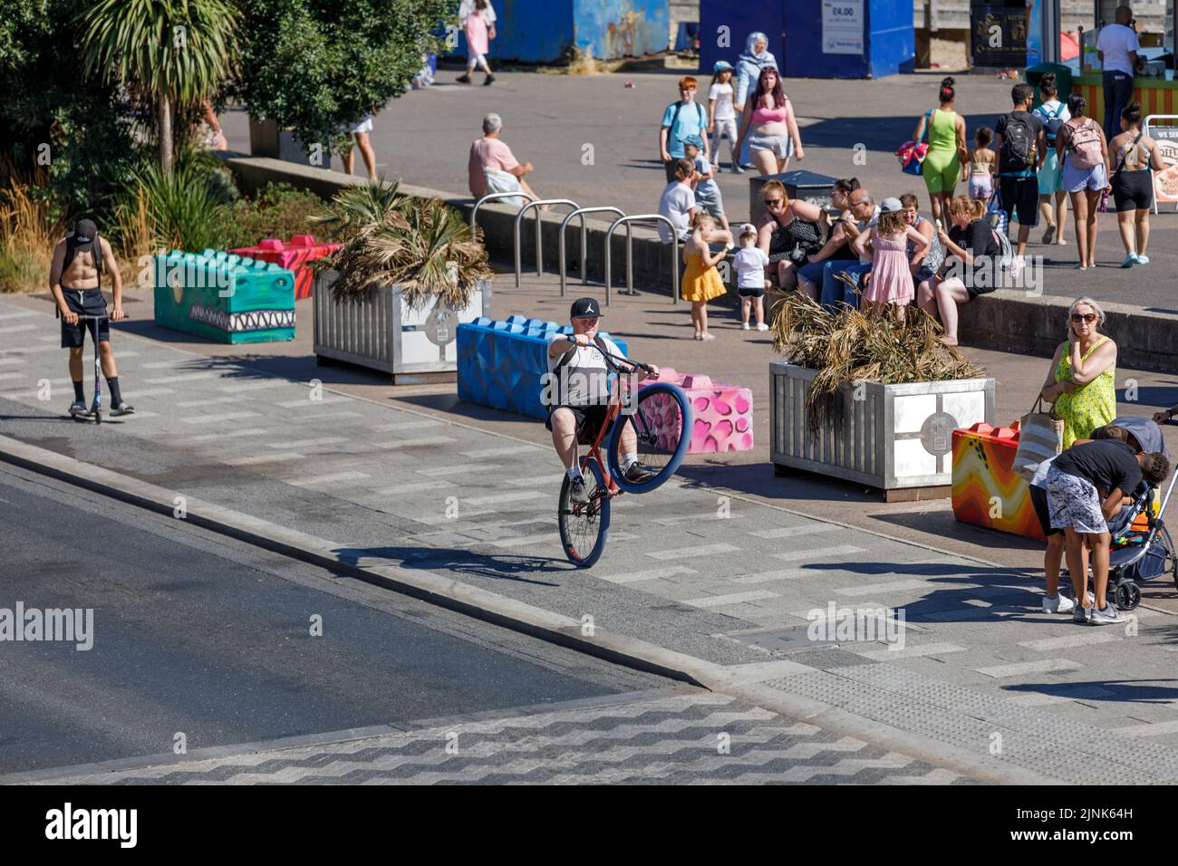 Teenager bike rider wheelies dangerously on one wheel past pedestrians ...