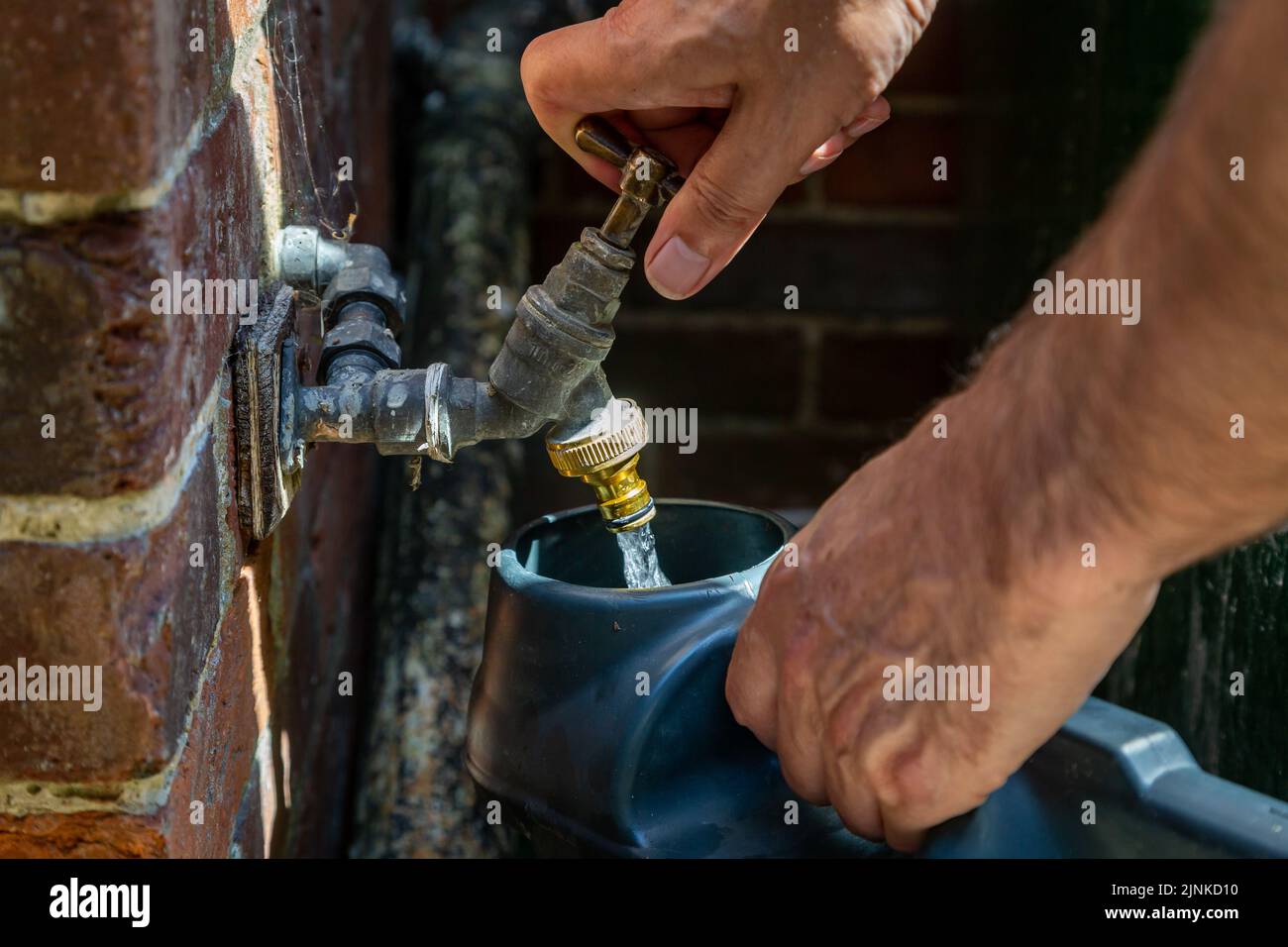 A man filling a watering can from an outside tap during a hosepipe ban ...