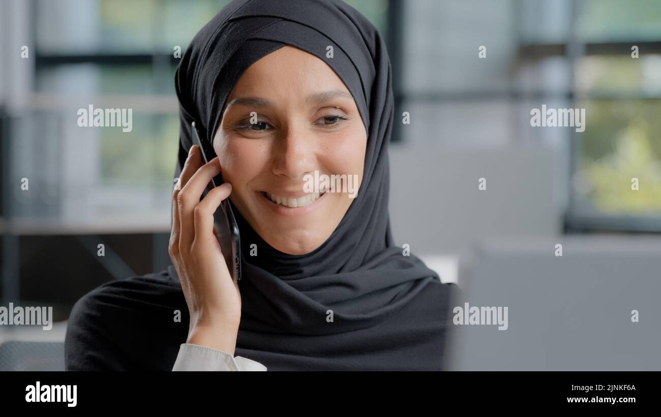 Close-up young smiling arab woman secretary in hijab talking on phone ...