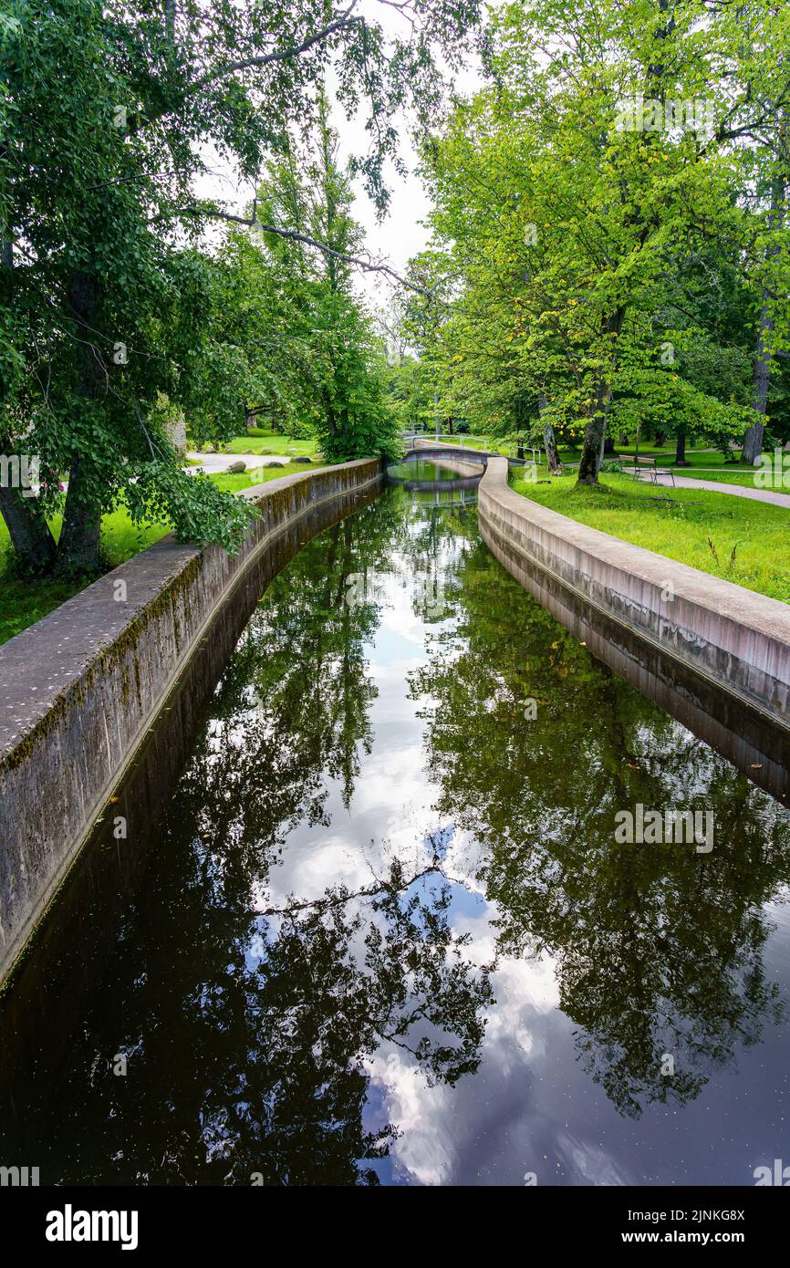 Small bridge over quiet water channel in the park next to large trees ...