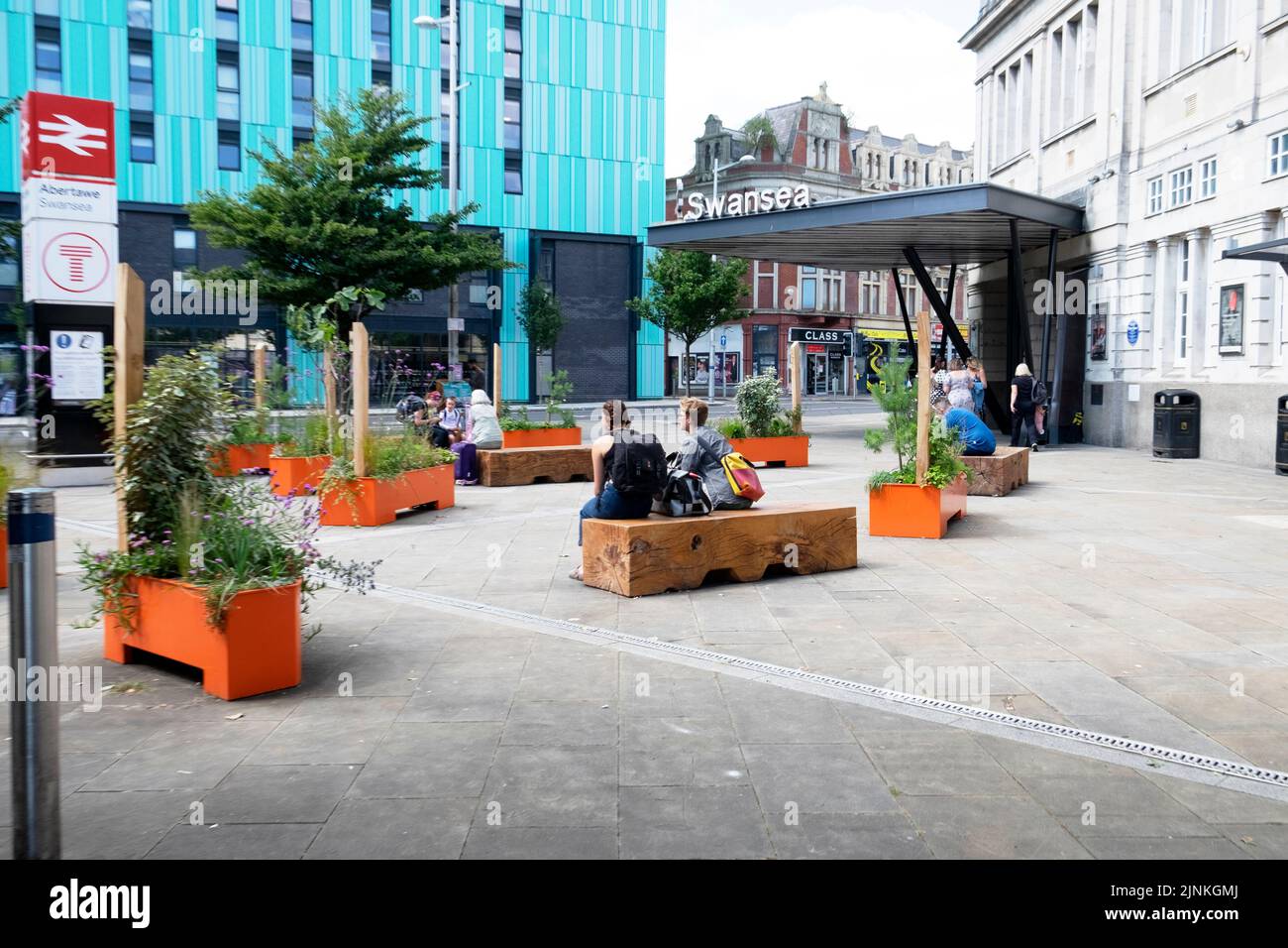 People sitting on wooden benches seats outside Swansea railway train ...