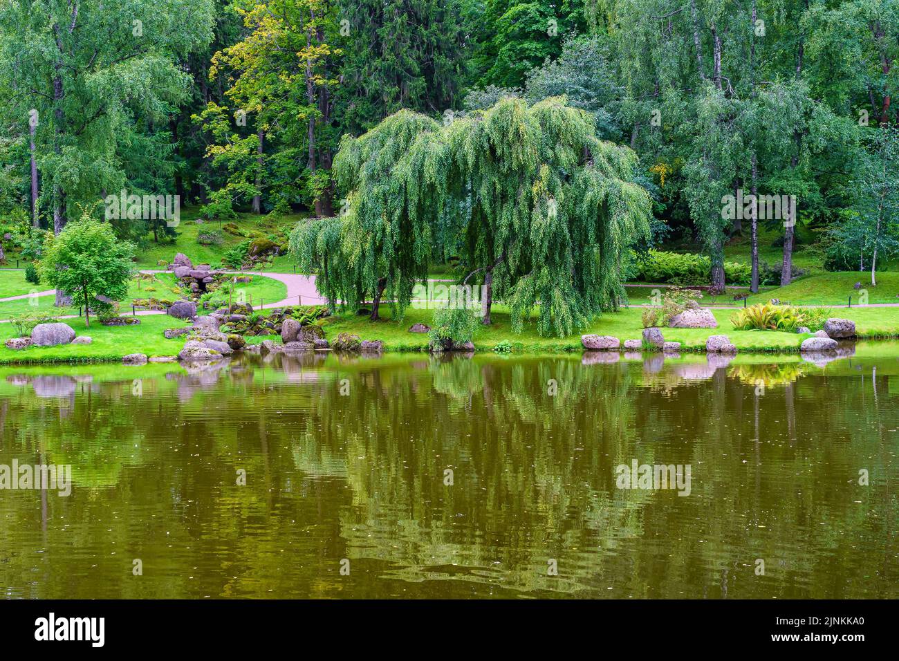 Japanese garden with lush trees that are reflected in the calm water of ...