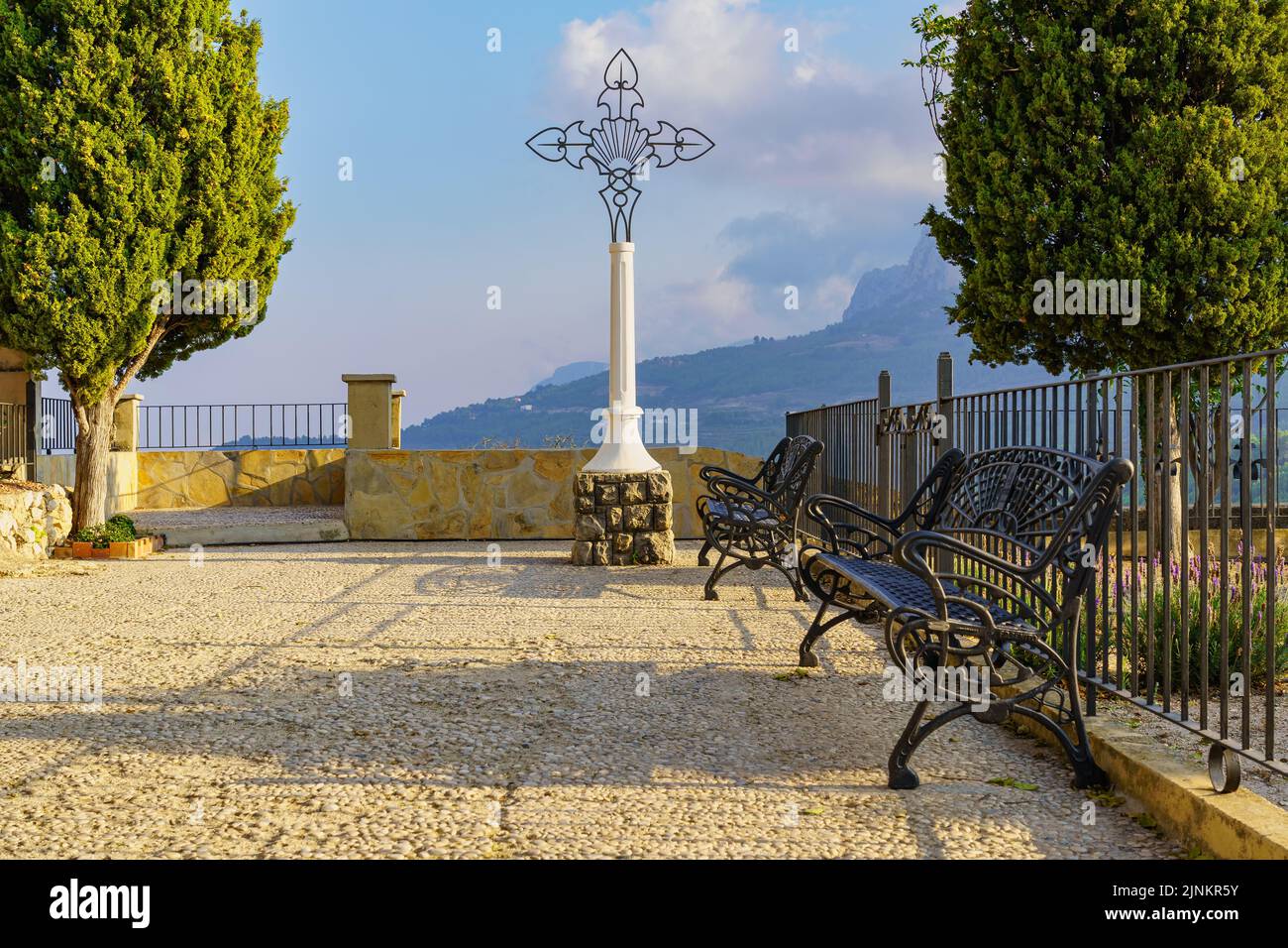 Christian cross in a public park with iron benches to rest and a ...