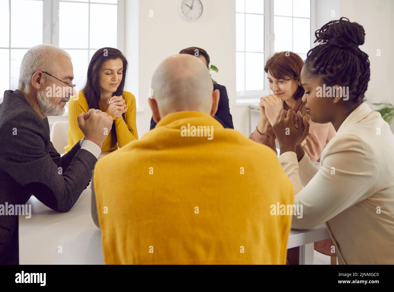 Diverse multicultural group of people sitting around table and praying ...