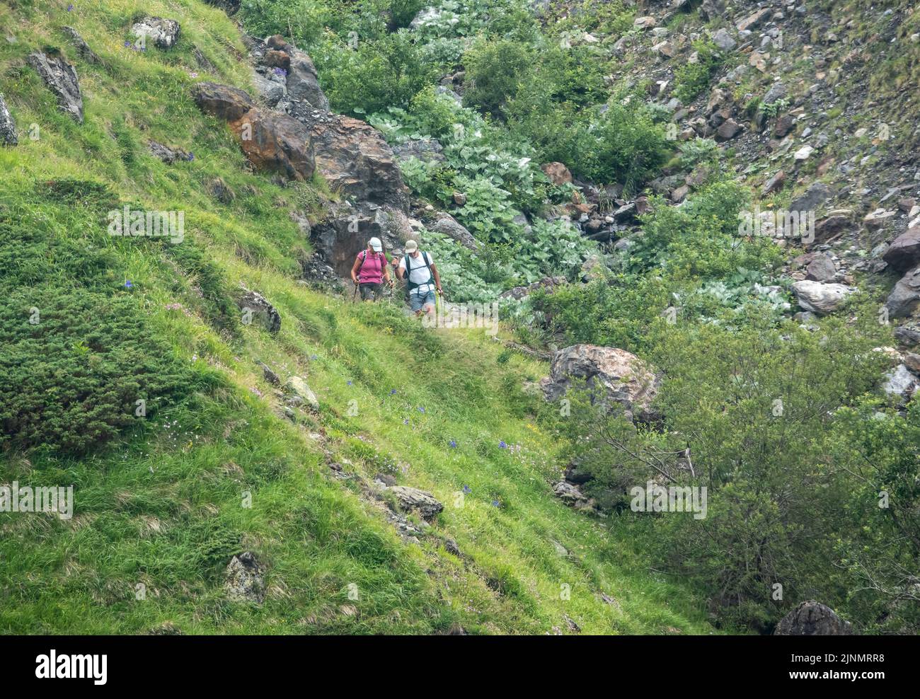 two trekkers passing in front of a massive mountain-side boulder Stock ...