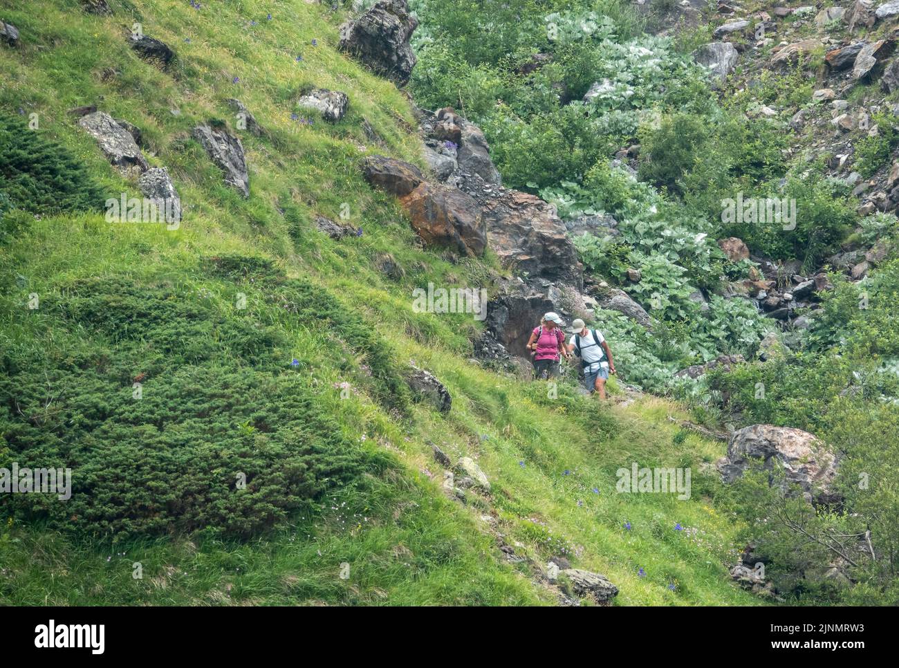 two trekkers passing in front of a massive mountain-side boulder Stock ...