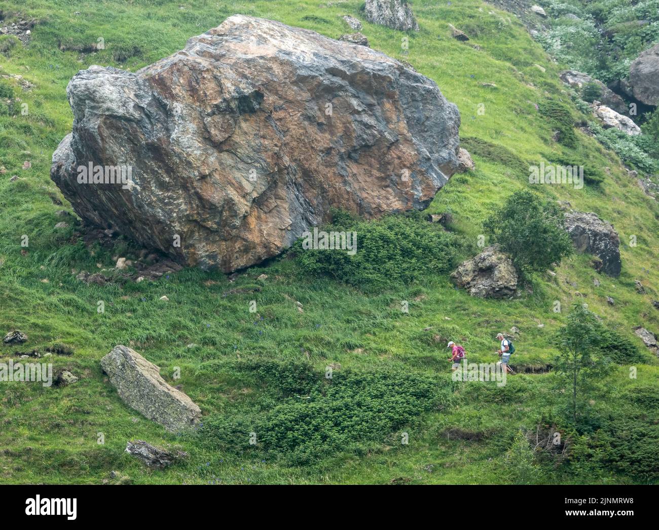 two trekkers passing in front of a massive mountain-side boulder Stock ...