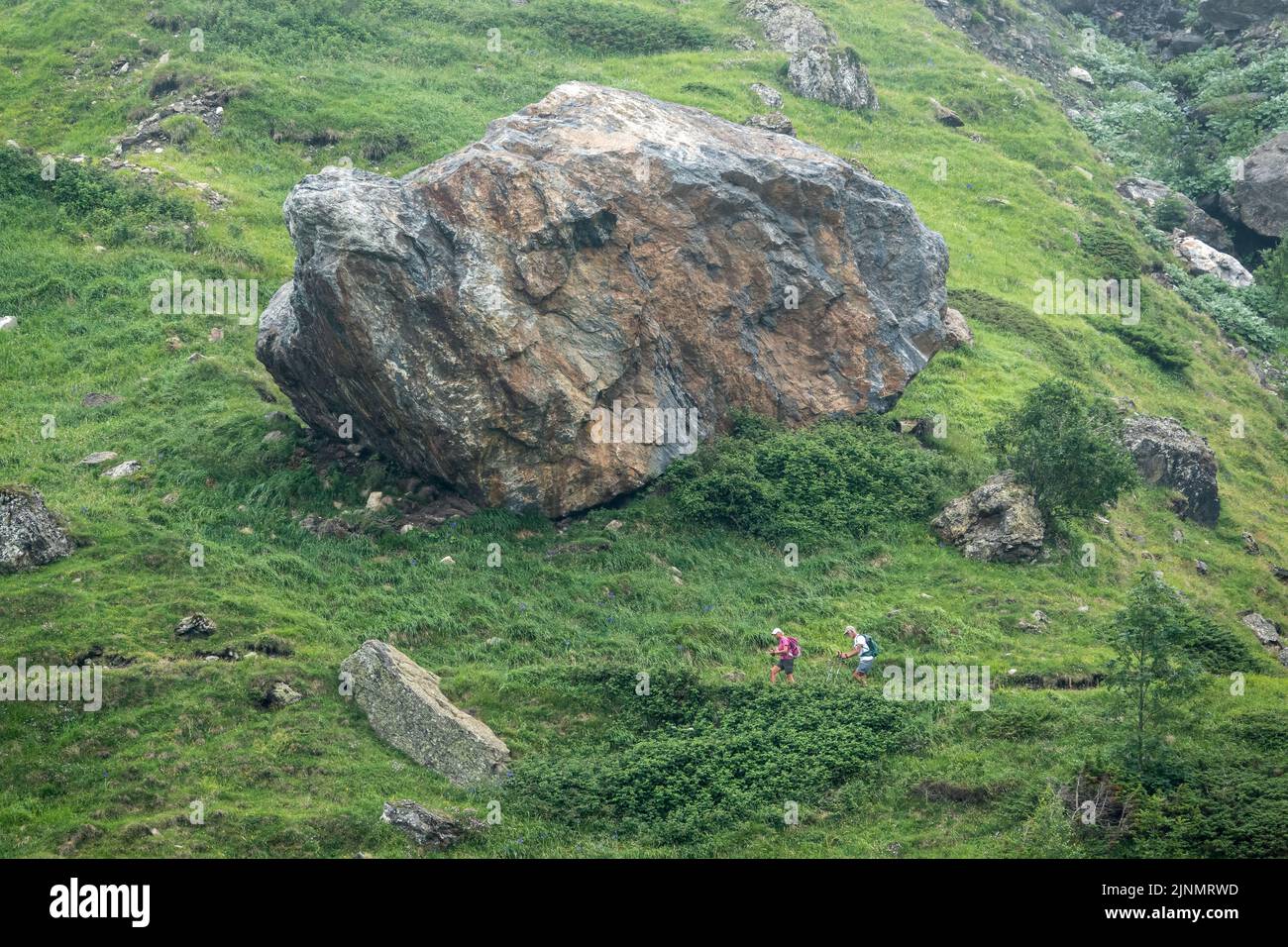 two trekkers passing in front of a massive mountain-side boulder Stock ...