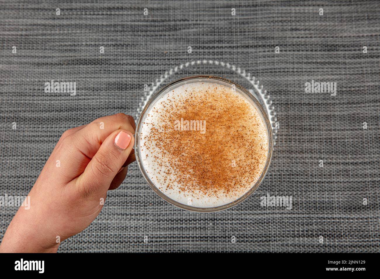 A woman's hand is holding a white cup of hot milk drink with cinnamon ...