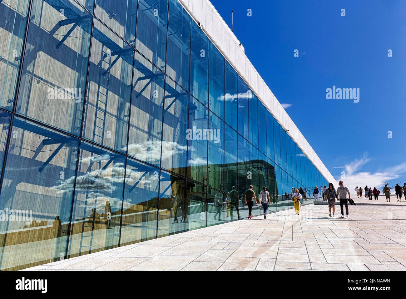 Pedestrians on the forecourt reflected in the glass facade of the opera ...