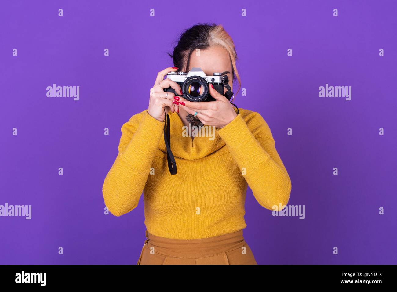 Attractive young lady taking a photo with her film camera over a violet ...
