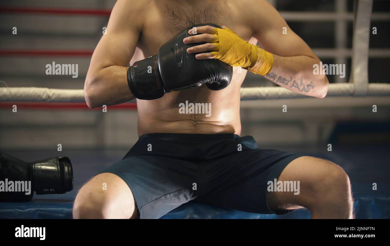 A tired man boxer sitting on the ring with one boxer glove on Stock ...