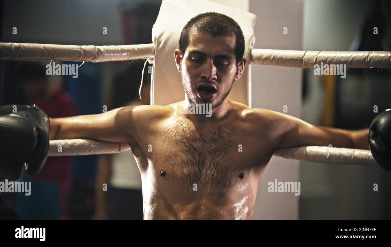 A tired man boxer sitting on the ring with a teeth guard in the mouth ...