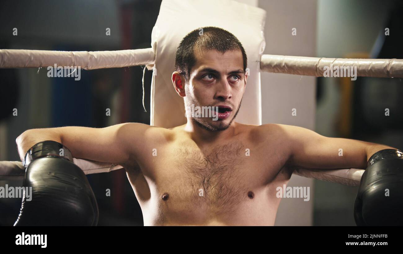 A man boxer sitting in the corner of the ring with a teeth guard in the ...