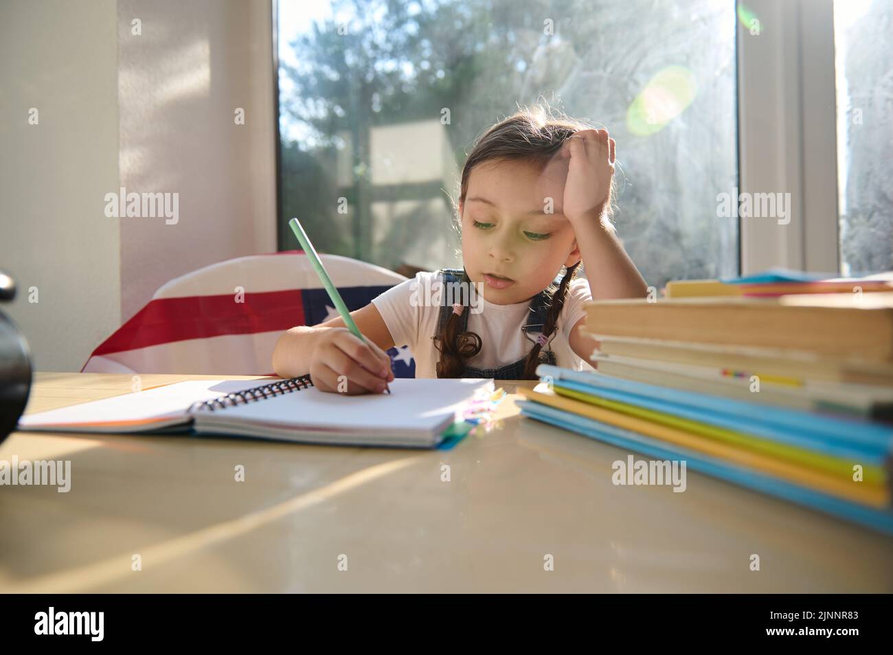 Adorable Caucasian child schoolgirl learns to write, makes notes in her ...