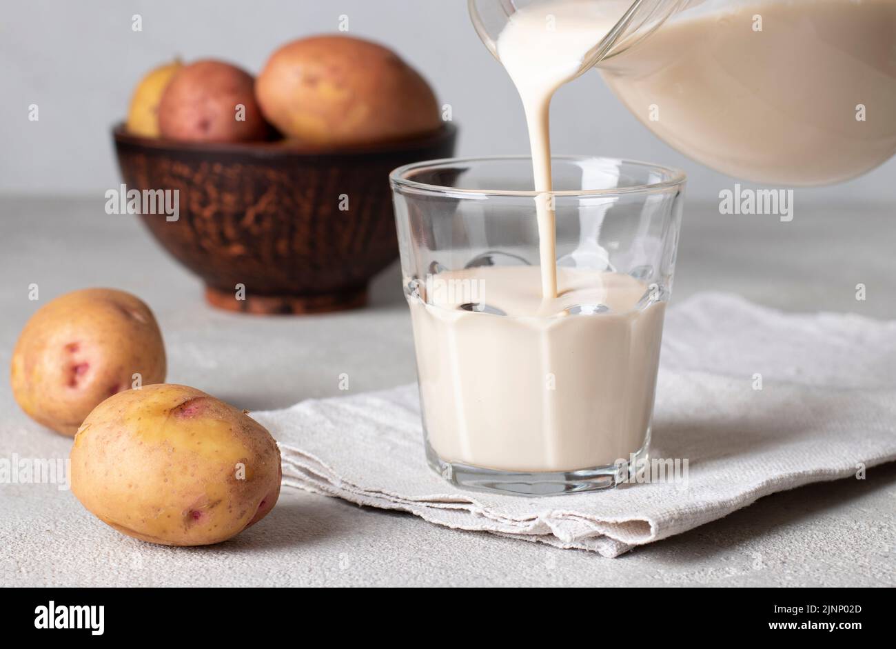 Vegan potato milk is poured into a glass from a jug. Use of plant-based ...