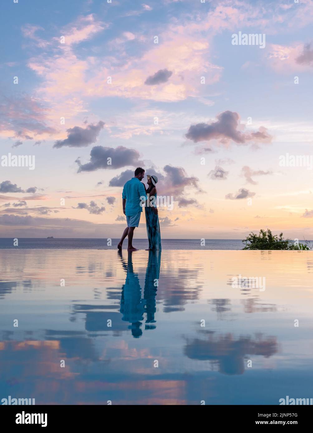 Young men and women watching the sunset with reflection in the infinity ...