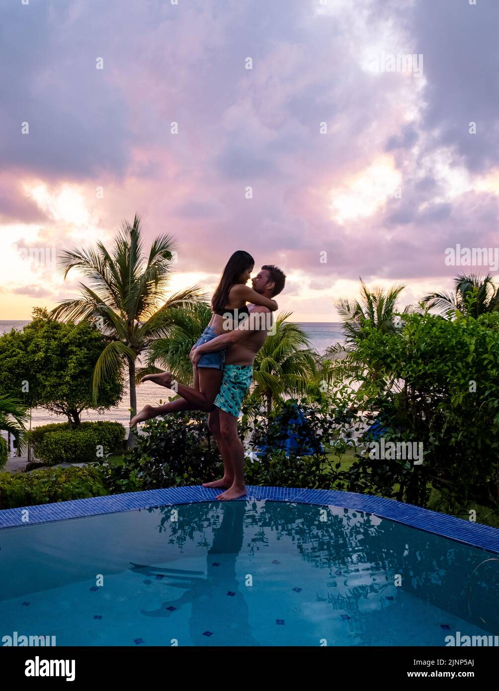 Young men and women watching the sunset in the infinity swimming pool ...