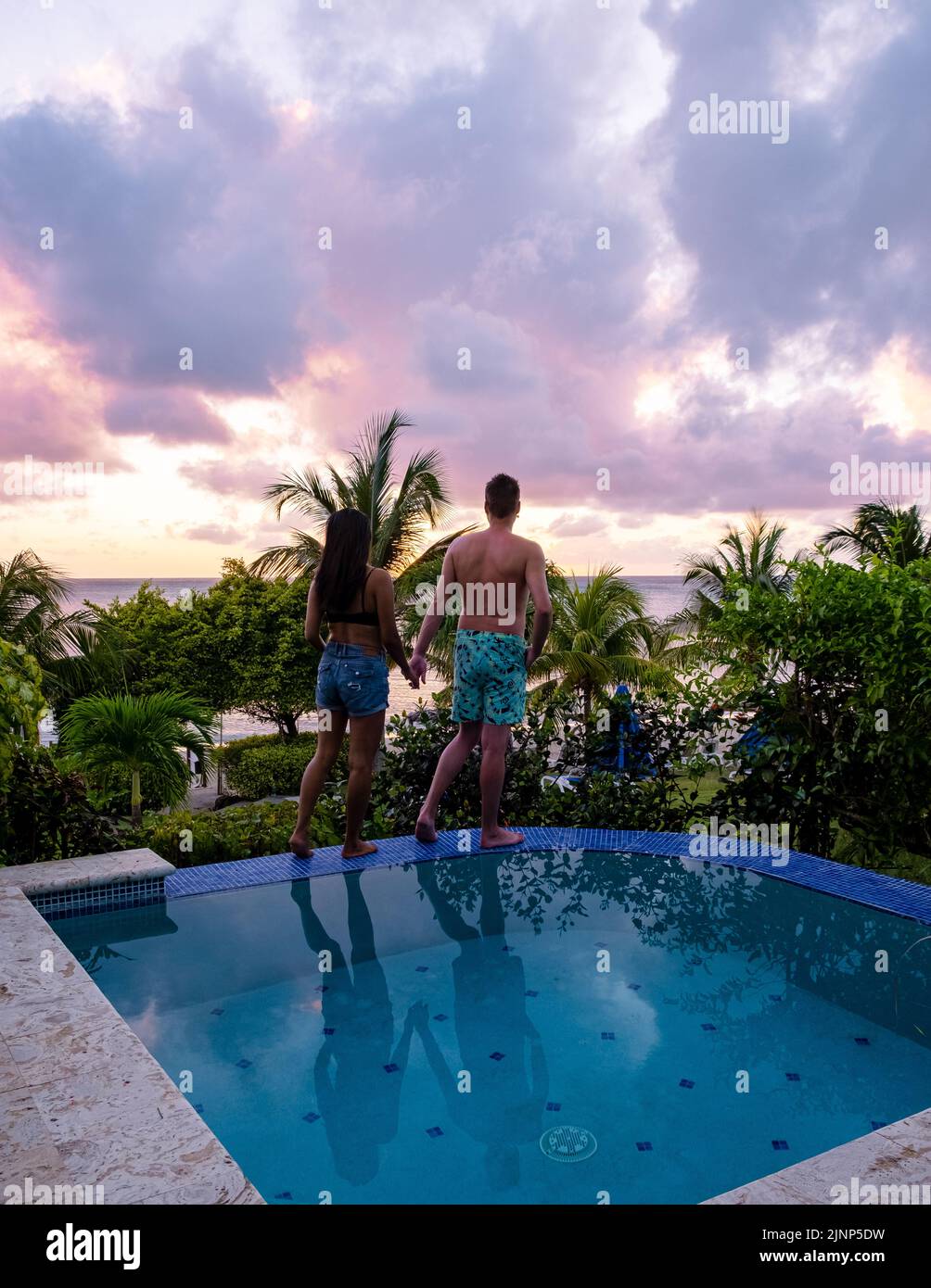 Young men and women watching the sunset in the infinity swimming pool ...