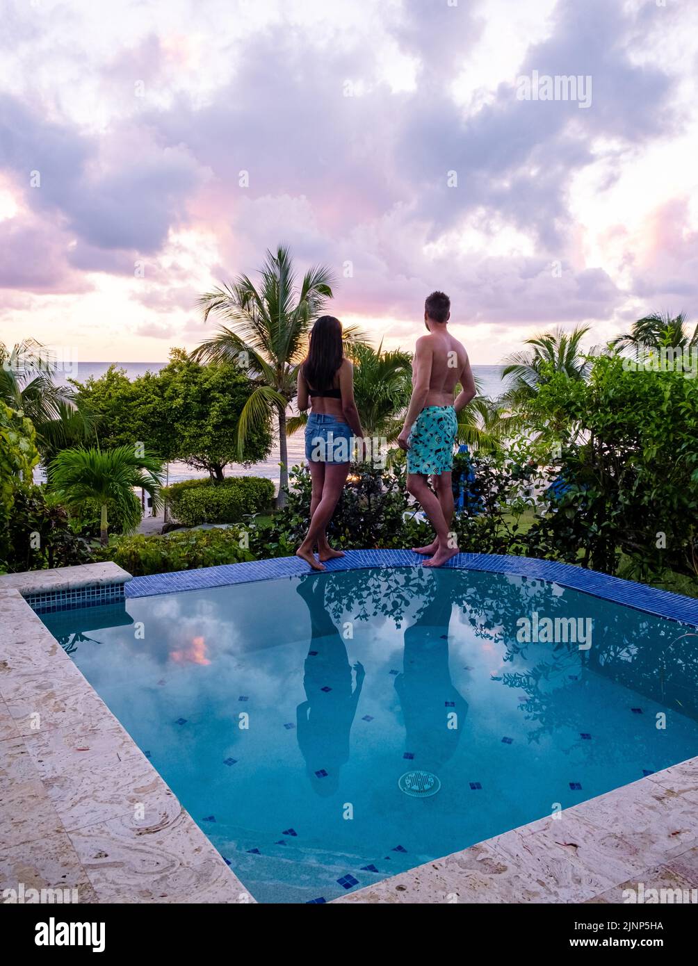 Young men and women watching the sunset in the infinity swimming pool ...