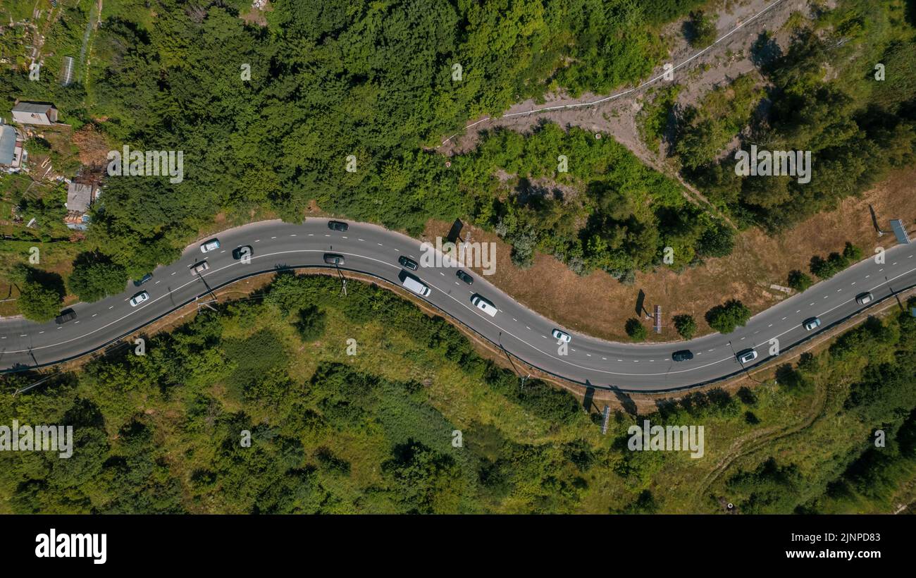 Aerial view of windy road passing through the green forest and mountain ...