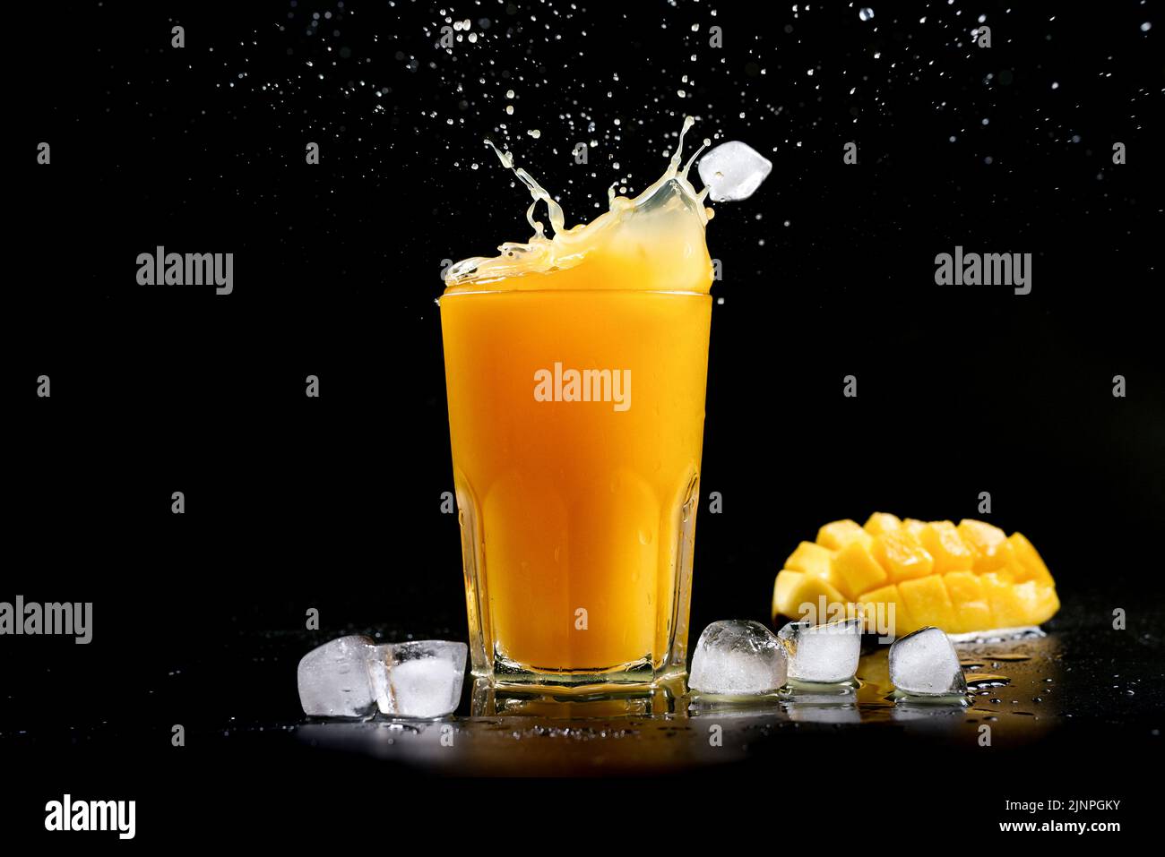 Fresh mango juice. A splash of mango cocktail on a black background. Ice cubes fall into the ...