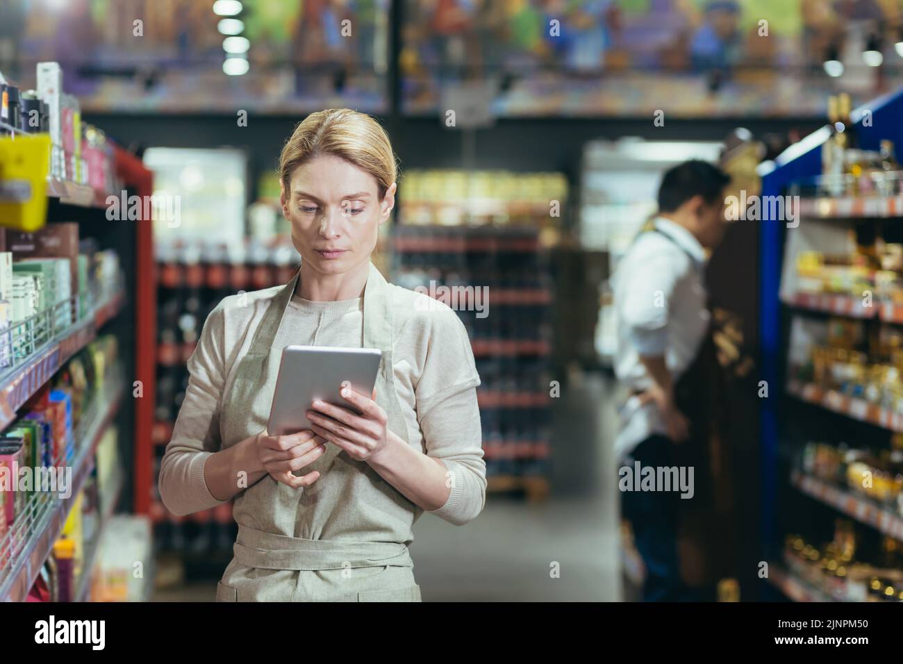 A woman seller in a supermarket uses a tablet computer to count the ...