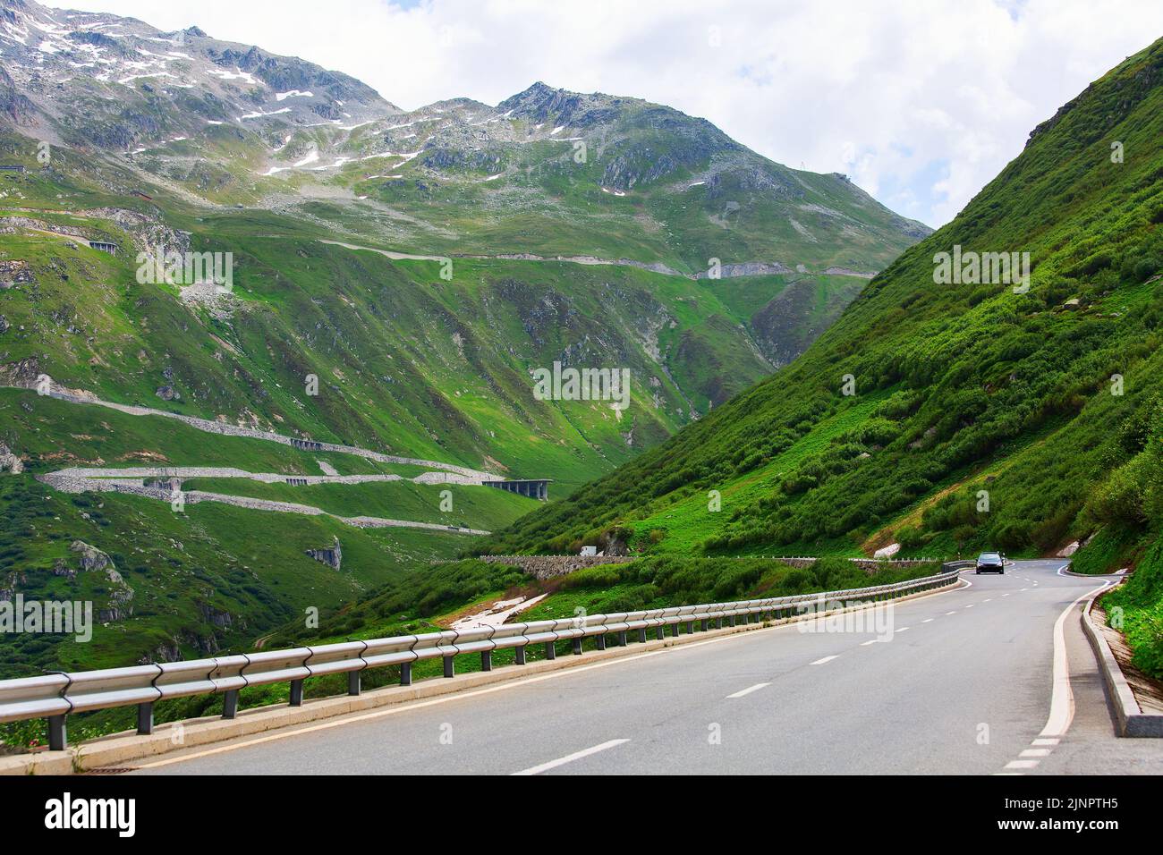 Furka pass in Swiss Alps in summer. A car drives along a winding ...