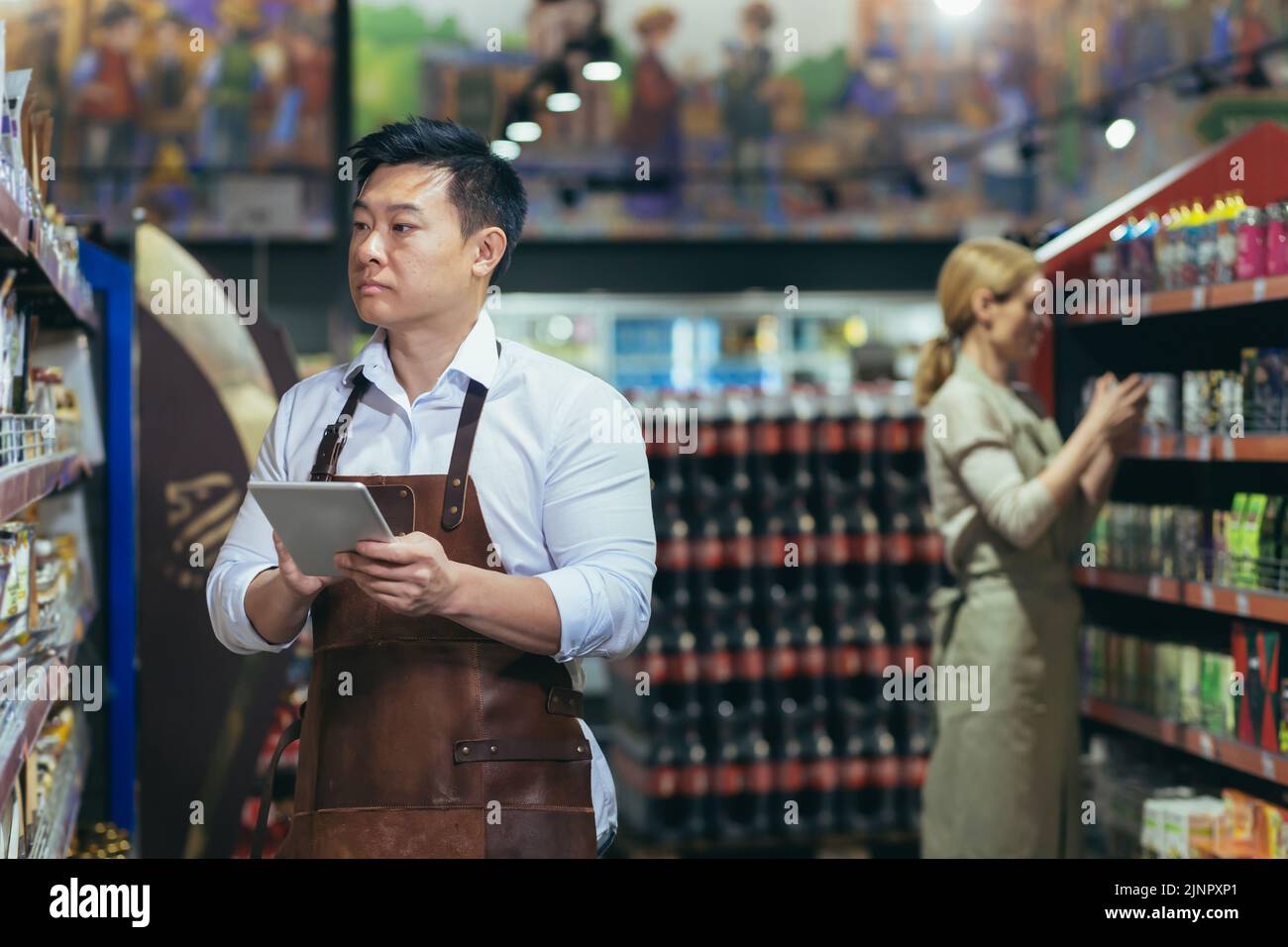 Two workers in a supermarket in the grocery department arrange products ...