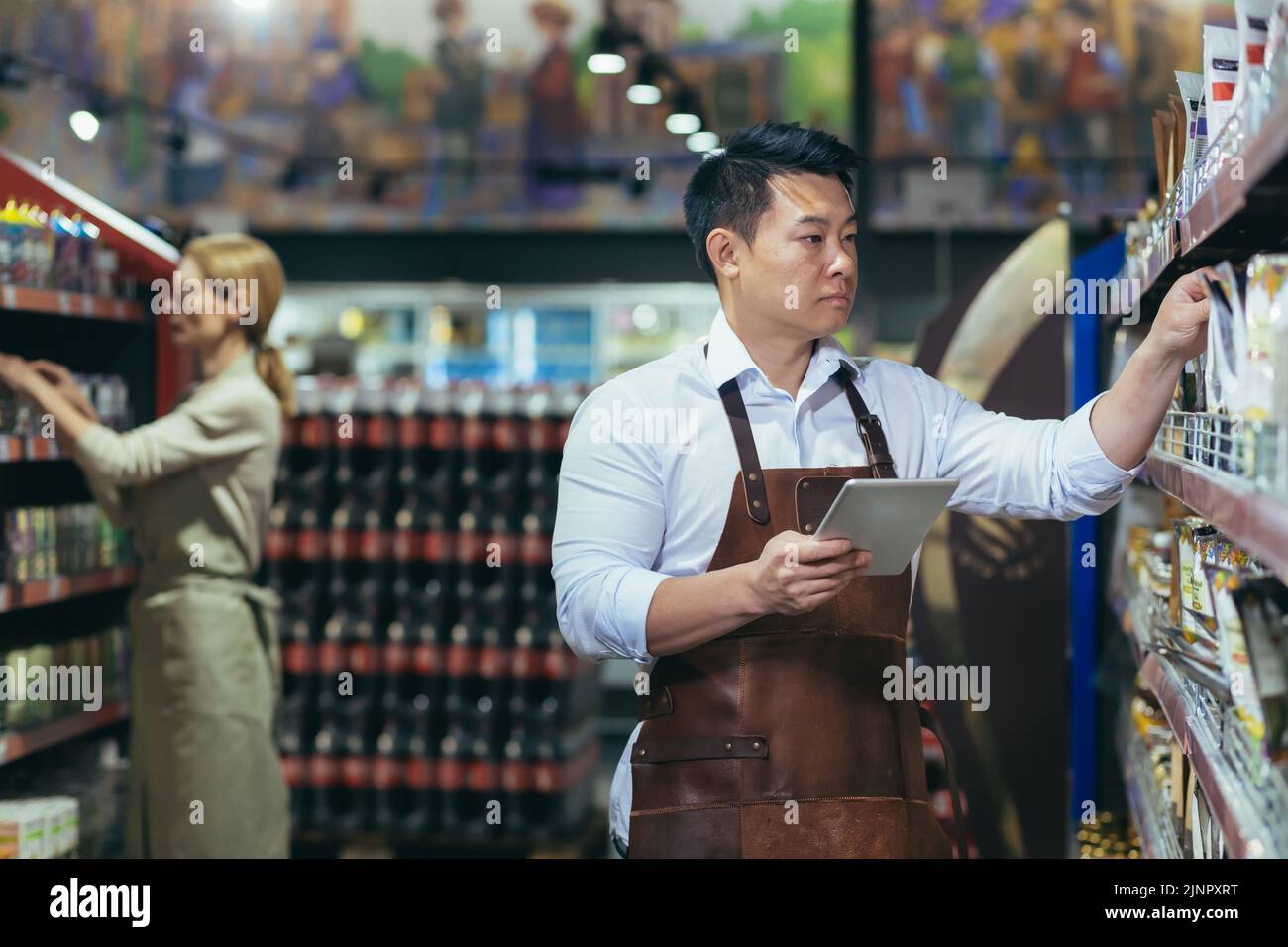 Two workers in a supermarket in the grocery department arrange products ...