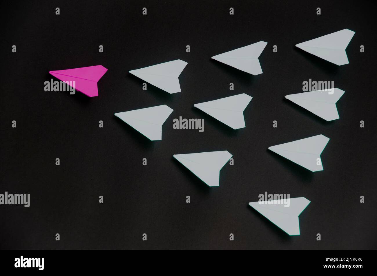 Purple paper plane origami leading white planes on dark background ...