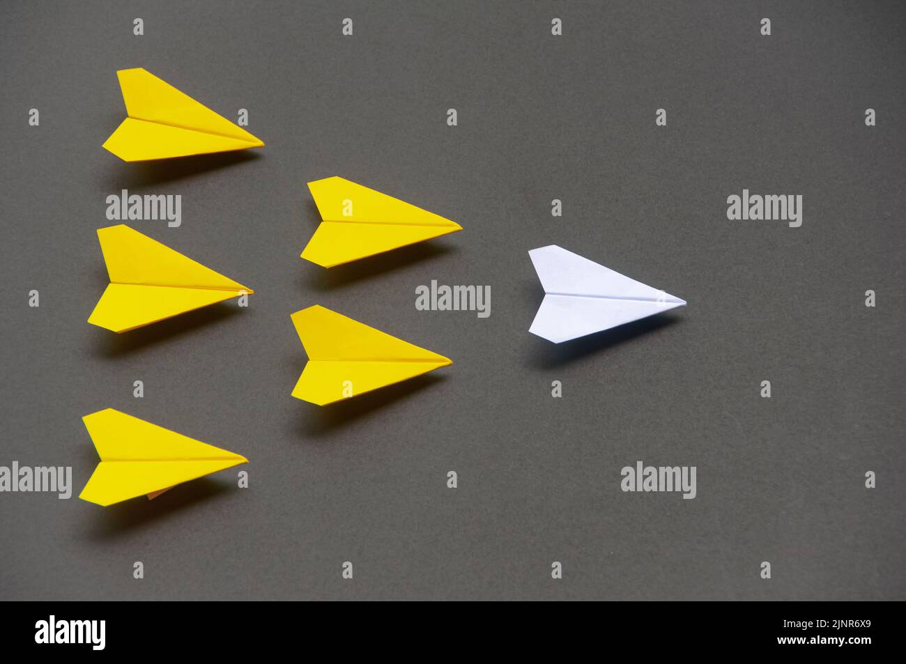 White paper plane origami leading yellow planes on dark background ...