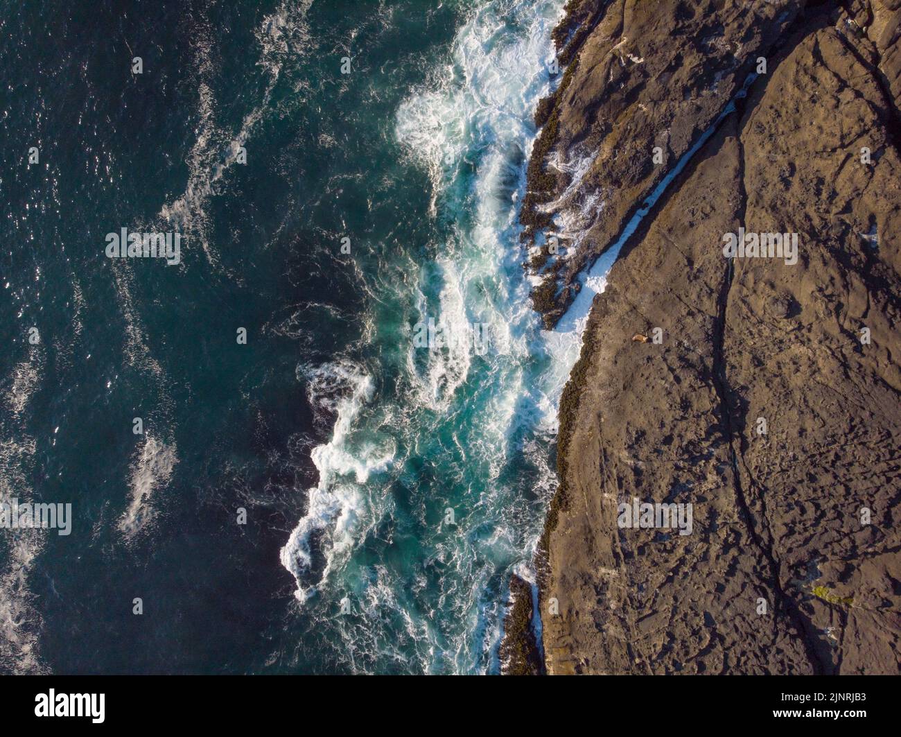 Top view of the raging ocean. White foamy waves break on a high stone ...