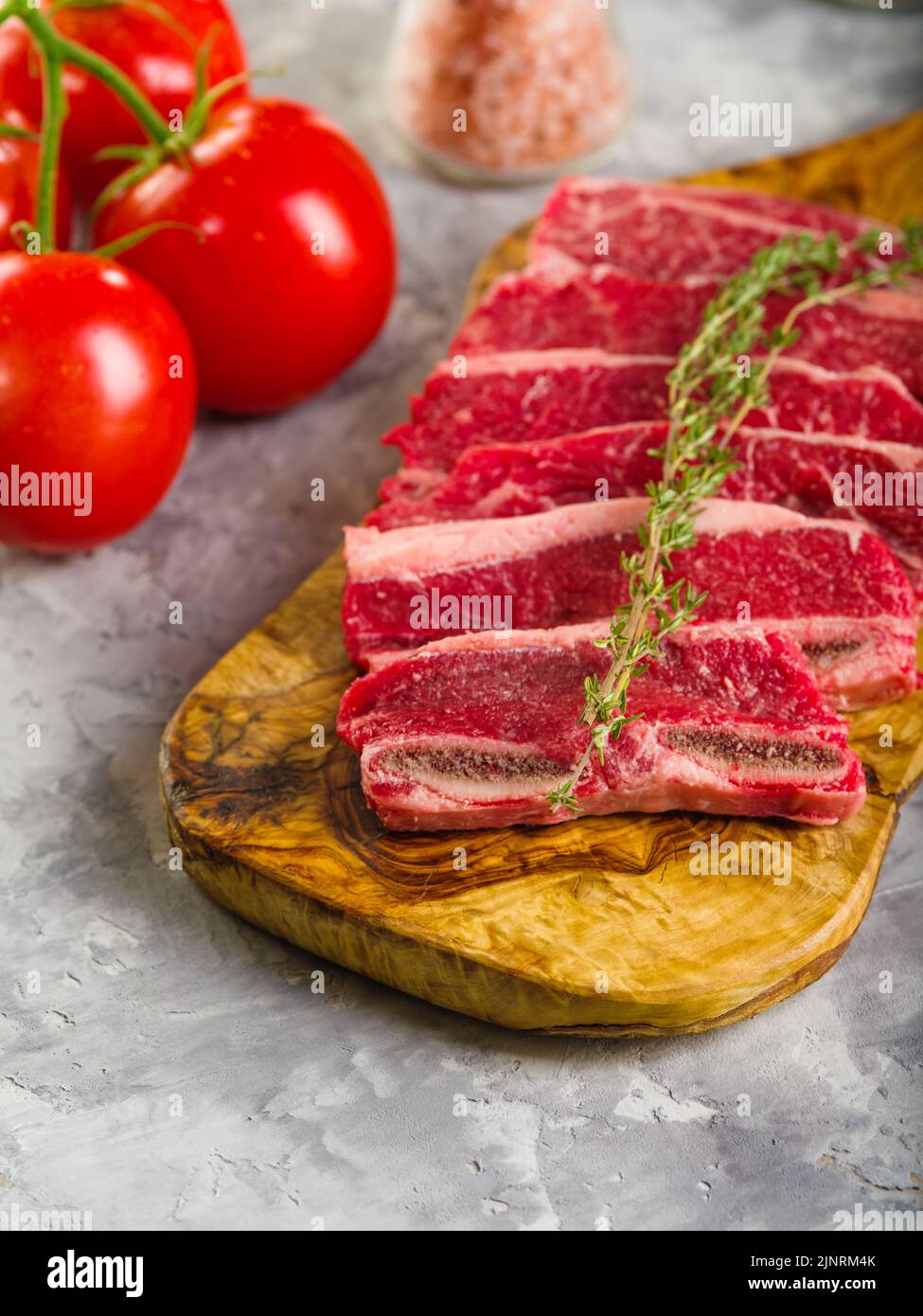 Raw steaks from organic farm meat on a cutting board and fresh tomatoes ...